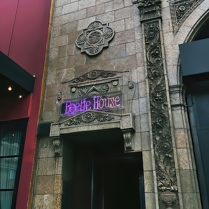 The purple neon "Beetle House" sign glows against stone walls like a gothic invitation. Tim Burton's spirit beckons from this architectural oddity on the LA streets.
