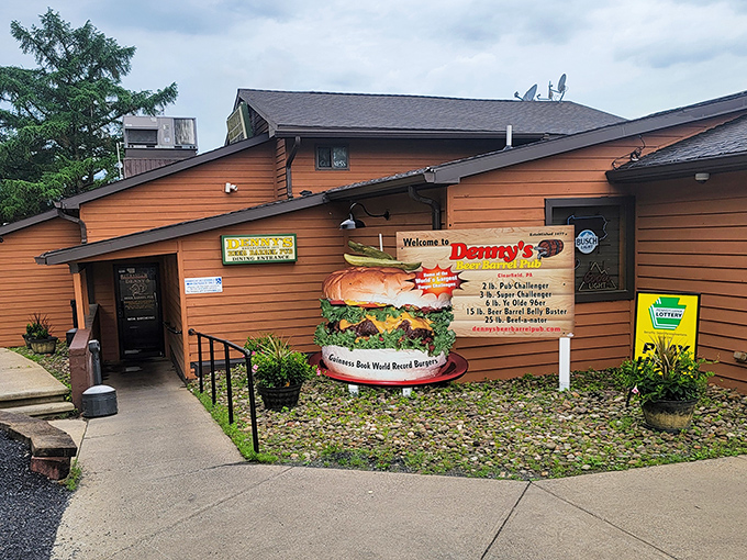 The rustic wooden exterior of Denny's Beer Barrel Pub promises burger adventures within, with a sign proudly displaying their legendary food challenges.