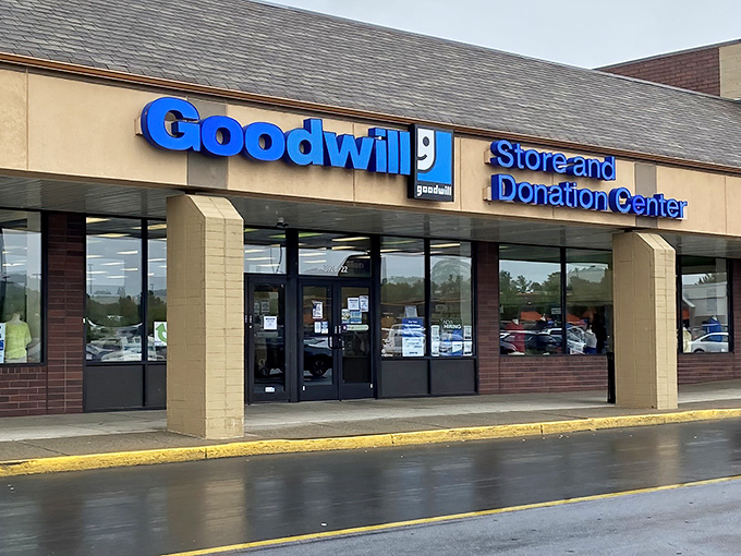 The blue Goodwill sign beckons like a lighthouse to treasure hunters. This unassuming storefront holds universes of possibility behind its doors.