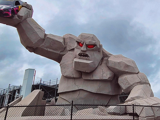 Miles the Monster emerges from the earth, concrete muscles flexed, with a race car hoisted triumphantly overhead like a trophy he's considering for lunch.