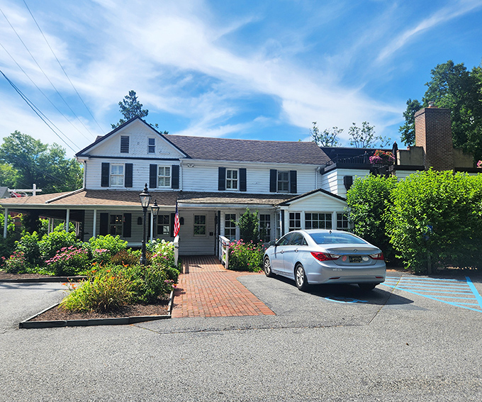 The historic white clapboard exterior of Buckley's Tavern welcomes you like an old friend, complete with lush greenery and that iconic red sign promising good times ahead.