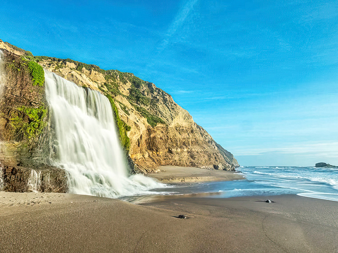 Nature's ultimate magic trick: a 40-foot waterfall that plunges directly onto the beach, catching golden hour light like it's auditioning for National Geographic.