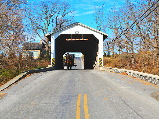 The classic white and red entrance of Eshleman's Mill Covered Bridge stands like a portal to simpler times, complete with an Amish buggy making its way through.