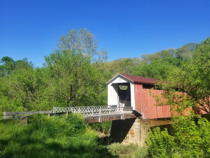 Nature's perfect frame for this classic red and white covered bridge, where the lush green hillsides of southeastern Ohio create a timeless postcard moment.