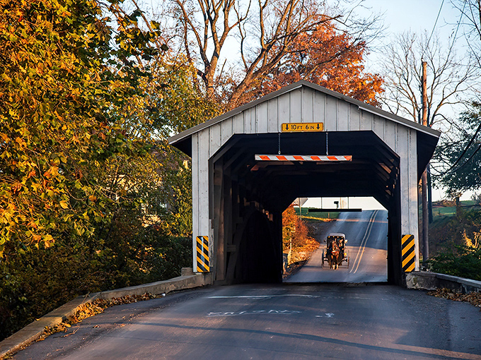 The classic white and red entrance of Eshleman's Mill Covered Bridge stands like a portal to simpler times, complete with an Amish buggy making its way through.