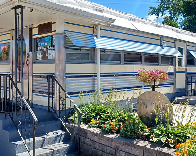 The classic silver exterior of Lawrence Park Dinor gleams in the sunlight, a time capsule of Americana with its distinctive blue trim and welcoming garden.