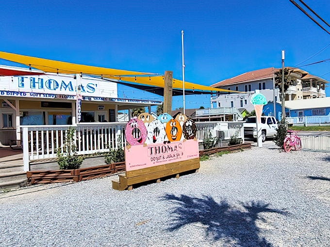 The cheerful storefront of Thomas' Donuts & Snack Shop, with its sunny yellow shade sails and whimsical donut character sign, invites passersby to indulge in sweet delights.