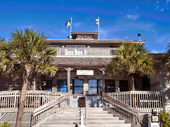The weathered wooden exterior of Peg Leg Pete's stands like a salty sea captain against Pensacola Beach's blue sky, pirate flags fluttering in welcome.