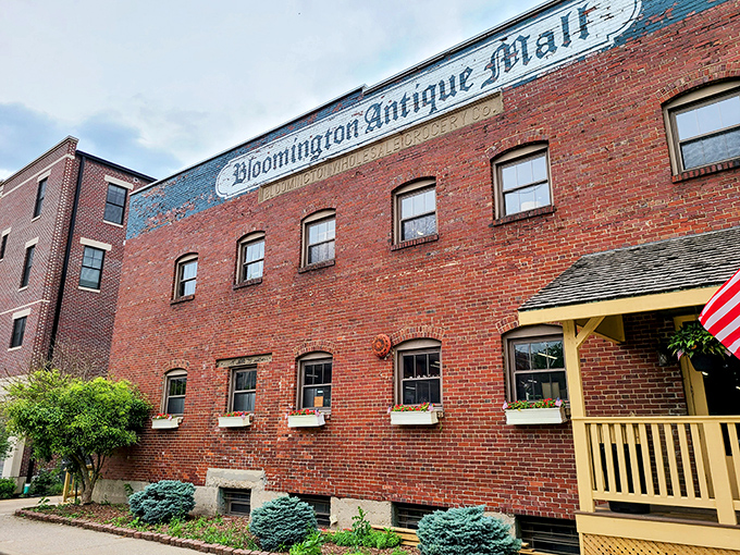 The brick facade of Bloomington Antique Mall stands like a time capsule with its cheerful yellow porch proudly announcing "WE ARE OPEN!" – an invitation to adventure.