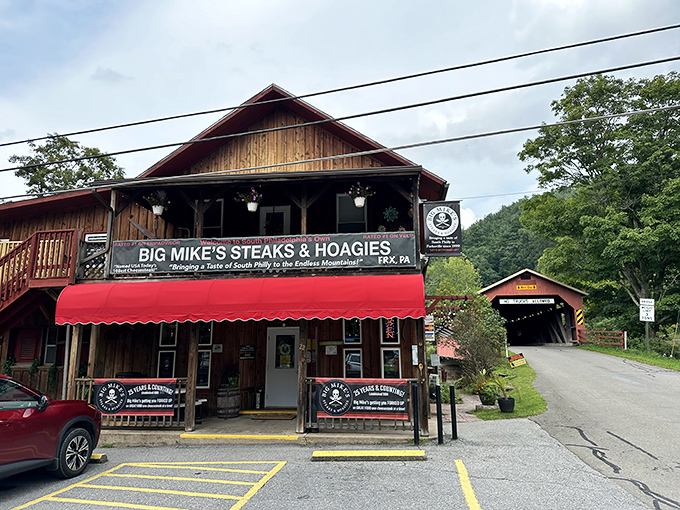 Rustic wooden charm meets sandwich paradise. Big Mike's stands proudly in Forksville with that iconic red awning, while a covered bridge peeks shyly from the right.