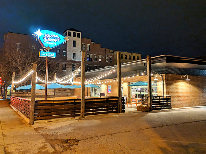 The welcoming facade of Pecan Penny's, where colorful flags flutter above a wooden patio fence like a backyard BBQ that got a serious upgrade.