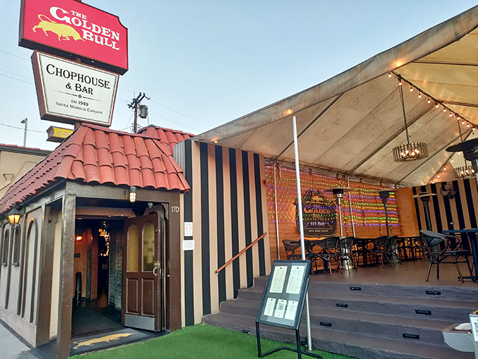 The iconic red sign beckons like a lighthouse for hungry souls. Spanish-style roof tiles and warm lighting promise an authentic California steakhouse experience.