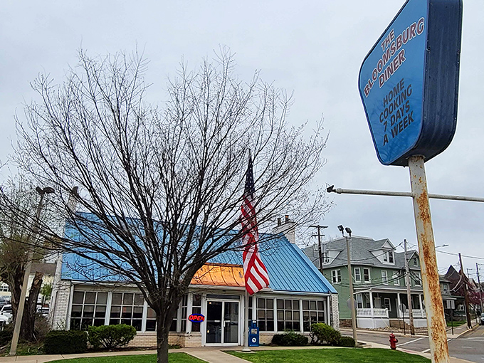 That iconic blue roof signals breakfast paradise like a beacon to hungry travelers. The American flag proudly announces: "Real diner food served here!"