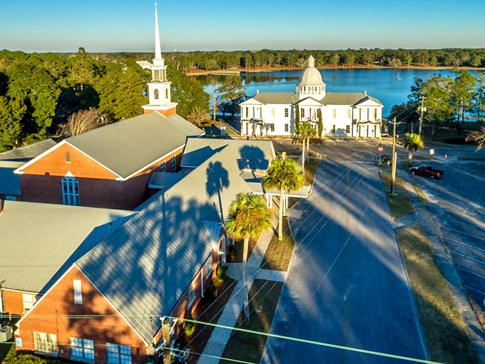 The perfect postcard moment: historic buildings surrounding Lake DeFuniak, where Victorian charm meets Florida sunshine in a scene straight out of a Hallmark movie.