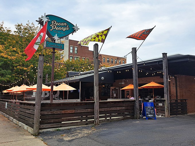 The welcoming facade of Pecan Penny's, where colorful flags flutter above a wooden patio fence like a backyard BBQ that got a serious upgrade.