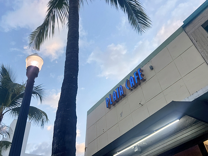 The unassuming exterior of Playa Cafe beckons with retro blue lettering and a palm tree guardian, proving Miami's best treasures don't need flashy neon to shine.