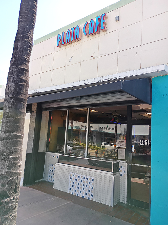 The unassuming exterior of Playa Cafe beckons with retro blue lettering and a palm tree guardian, proving Miami's best treasures don't need flashy neon to shine.