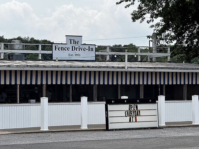 The iconic blue and white striped awning of The Fence Drive-In stands as a beacon to hungry travelers, promising simple pleasures and legendary fish.