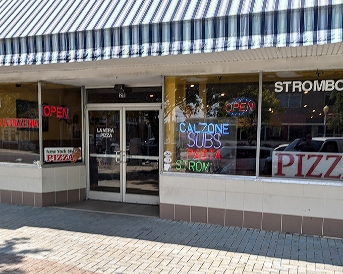 The blue and white striped awning of La Vera Pizzeria stands as a beacon of hope for the pizza-deprived. No frills, just neon promises of deliciousness within.