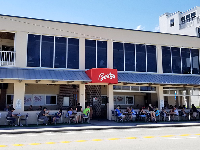 The iconic red "Boston's" sign beckons hungry travelers like a lighthouse for seafood lovers. Beach proximity and cold beer await just beyond those doors.