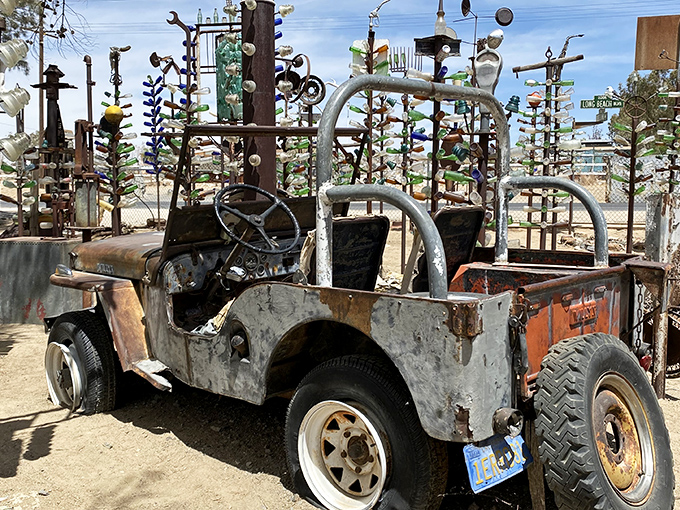 An automotive time capsule sits among metal trees adorned with colorful bottles, like some desert mirage where vehicles come to retire with dignity.