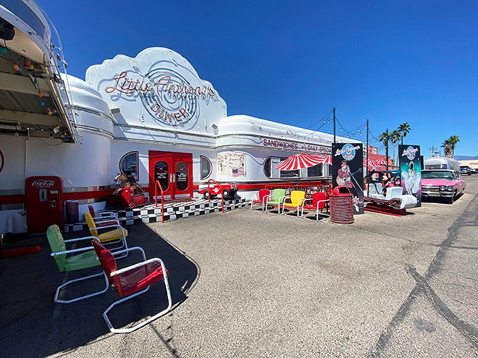 The gleaming white exterior of Little Anthony's Diner beckons like a time portal to the 1950s, complete with colorful retro chairs and classic car.
