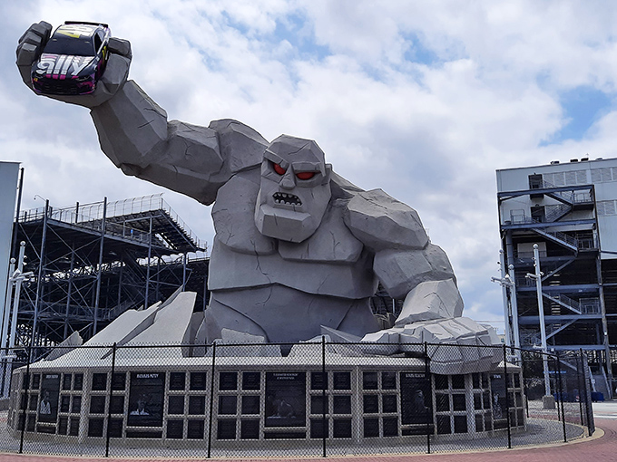 Miles the Monster emerges from the earth, concrete muscles flexed, with a race car hoisted triumphantly overhead like a trophy he's considering for lunch.