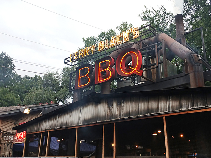 The neon BBQ sign glows like a smoky beacon of hope for hungry travelers. Terry Black's industrial-chic exterior promises no frills&mdash;just exceptional barbecue worth the journey.