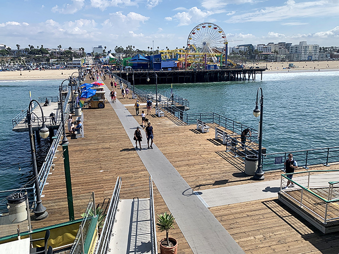 The wooden walkway stretches toward infinity, where cotton candy skies meet Pacific blues and the Ferris wheel stands sentinel over California dreams.