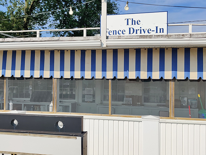 The iconic blue and white striped awning of The Fence Drive-In stands as a beacon to hungry travelers, promising simple pleasures and legendary fish.