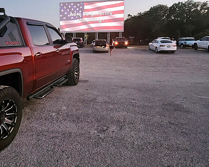 The American flag glows on screen as pickup trucks and sedans settle in for showtime. Movie magic meets patriotic pride under the Florida stars.
