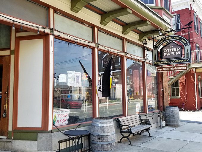 The charming storefront of The Other Farm beckons with its classic Pennsylvania brick facade, wooden bench, and barrel planters&mdash;small-town Americana at its most inviting.