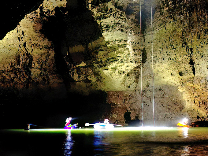 Explorers glide across the emerald waters of Devil's Well, their kayaks illuminated like alien spacecraft beneath the cathedral-like cavern ceiling.