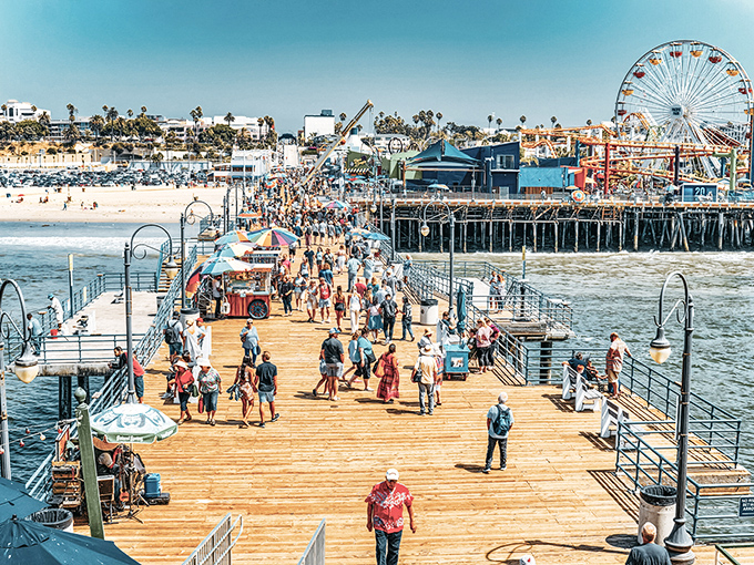 The wooden walkway stretches toward infinity, where cotton candy skies meet Pacific blues and the Ferris wheel stands sentinel over California dreams.