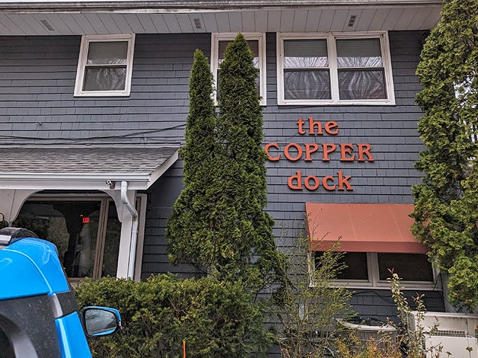 The blue-gray shingled exterior with bright orange signage feels like discovering a secret lakeside hideaway that locals have been keeping to themselves.