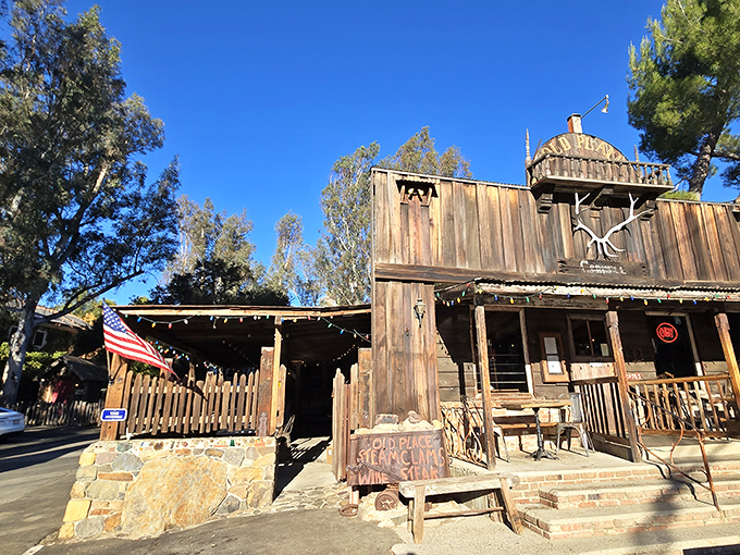 The Old Place stands defiant against time, its weathered wood and rustic tower beckoning hungry travelers like a frontier outpost for modern appetites.