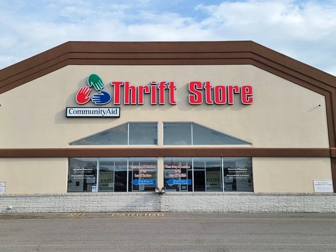 The welcoming facade of CommunityAid beckons treasure hunters with its distinctive red signage and colorful hand logo, promising adventures in secondhand shopping.