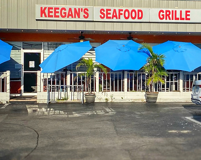 The unassuming exterior of Keegan's Seafood Grille, where those vibrant blue umbrellas hint at the coastal treasures waiting inside.