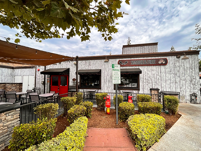 The weathered wood exterior of Smoke And Fire beckons like a rustic oasis in Riverside, promising smoky treasures behind that bright red door.