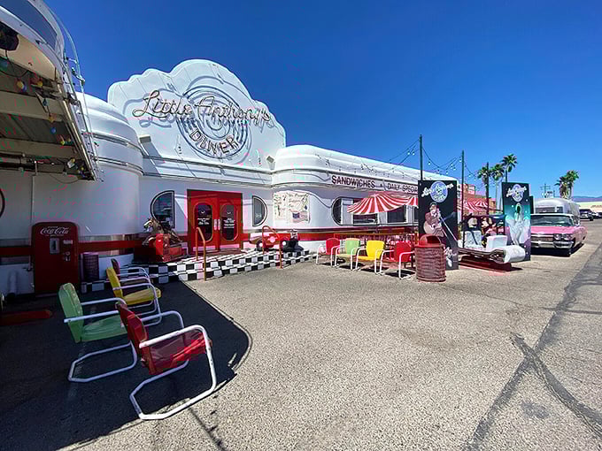The gleaming white exterior of Little Anthony's Diner beckons like a time portal to the 1950s, complete with colorful retro chairs and classic car.
