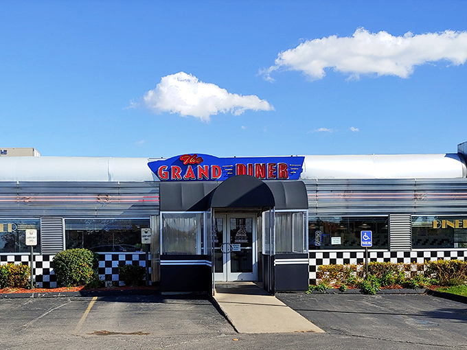 The gleaming silver exterior of The Grand Diner beckons like a time machine to the golden age of roadside Americana. Those checkered accents promise authentic diner magic inside.
