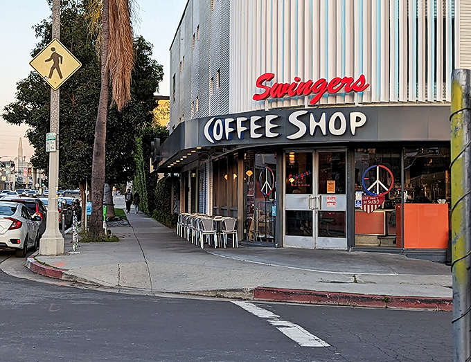 The iconic corner entrance of Swingers, where the neon sign and peace symbols promise both nostalgia and pancakes worth crossing Beverly Boulevard for.