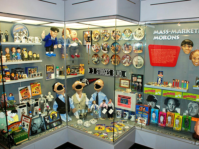 The "Mass-Marketed Morons" exhibit showcases decades of Stooge collectibles, from bobbleheads to puppets, celebrating America's beloved pie-throwing pioneers.