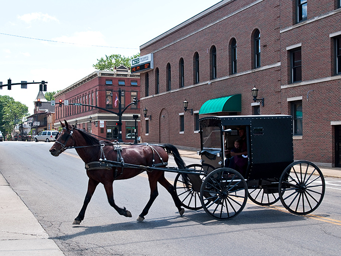 The quintessential Amish Country moment: a horse-drawn buggy clip-clops past historic brick buildings in downtown Millersburg, where modern life respectfully shares the road with tradition. 
