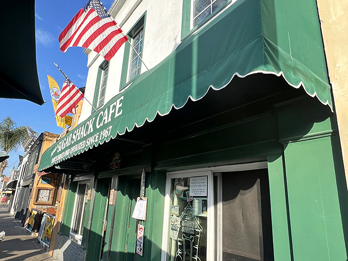 The iconic green awning of Sugar Shack Cafe stands as a beacon of breakfast hope on Huntington Beach's Main Street, American flags fluttering above like culinary patriotism.