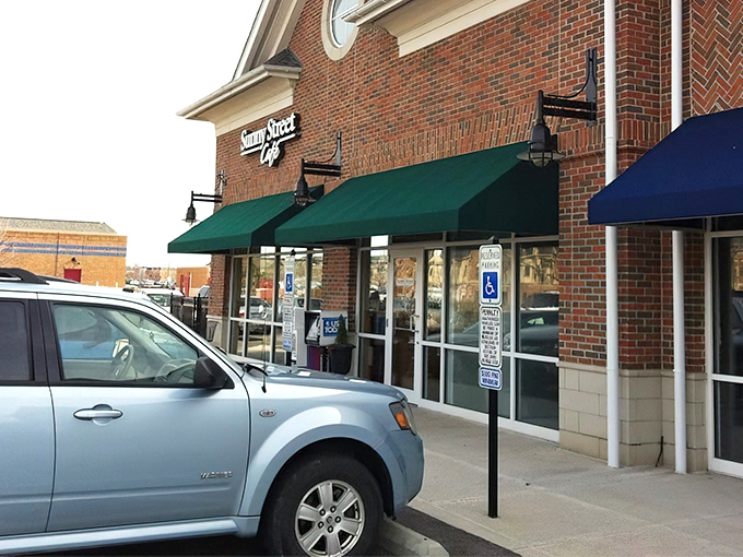 The unassuming brick exterior of Sunny Street Caf&eacute;, where culinary magic happens behind those modest green awnings. Breakfast nirvana awaits!