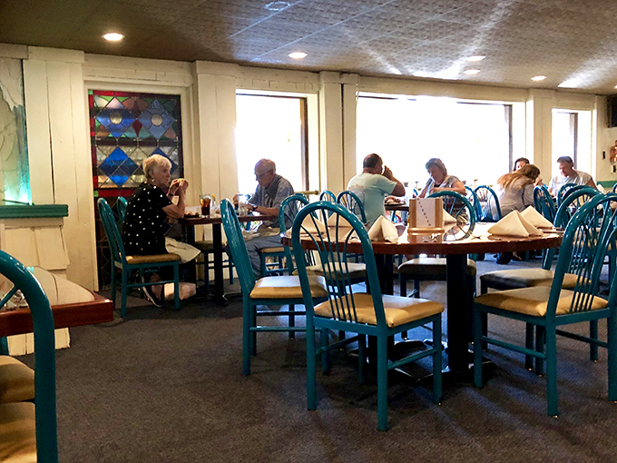 Generations gather around turquoise chairs, proof that the best family traditions often involve passing the butter and stories simultaneously.