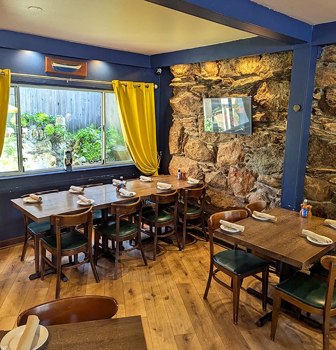 Stone walls and wooden tables create a dining room that feels like a secret coastal hideaway. Those yellow curtains are sunshine on standby.