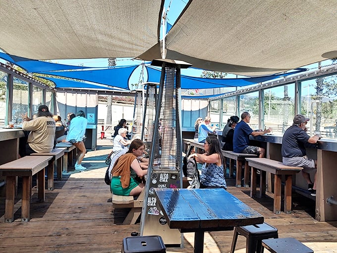Community tables under blue sail shades&mdash;where strangers become friends over shared taco appreciation and ocean breezes.