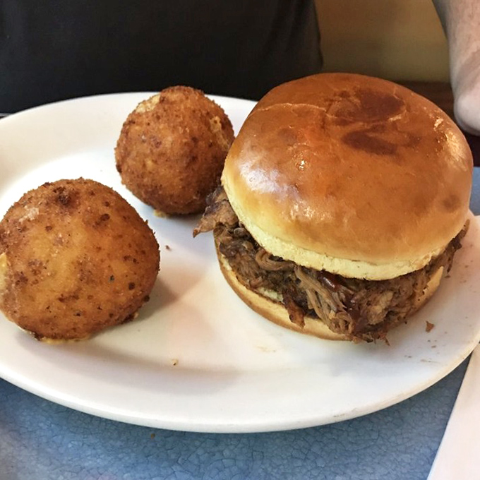 A pulled pork sandwich flanked by hush puppies &ndash; the kind of plate that makes you want to high-five the chef.